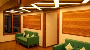 Quarto de hotel moderno com sofá verde, decoração de parede em painéis de madeira e luminárias geométricas no teto.
