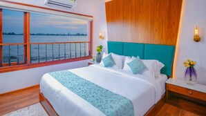 Quarto com uma grande janela com vista para a água, cama com cabeceira verde-água e mesa de cabeceira com um vaso de flores.