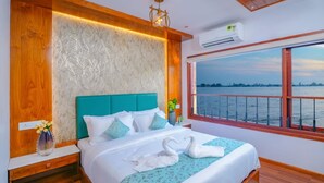 Quarto com uma grande janela, cama com roupa de cama branca e vista para a água.