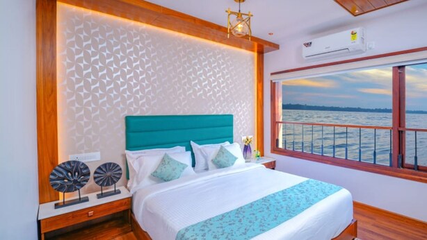 Quarto com uma janela ampla que oferece vista para a água, cama com roupa de cama branca e detalhes verde-água, e arte decorativa na parede.