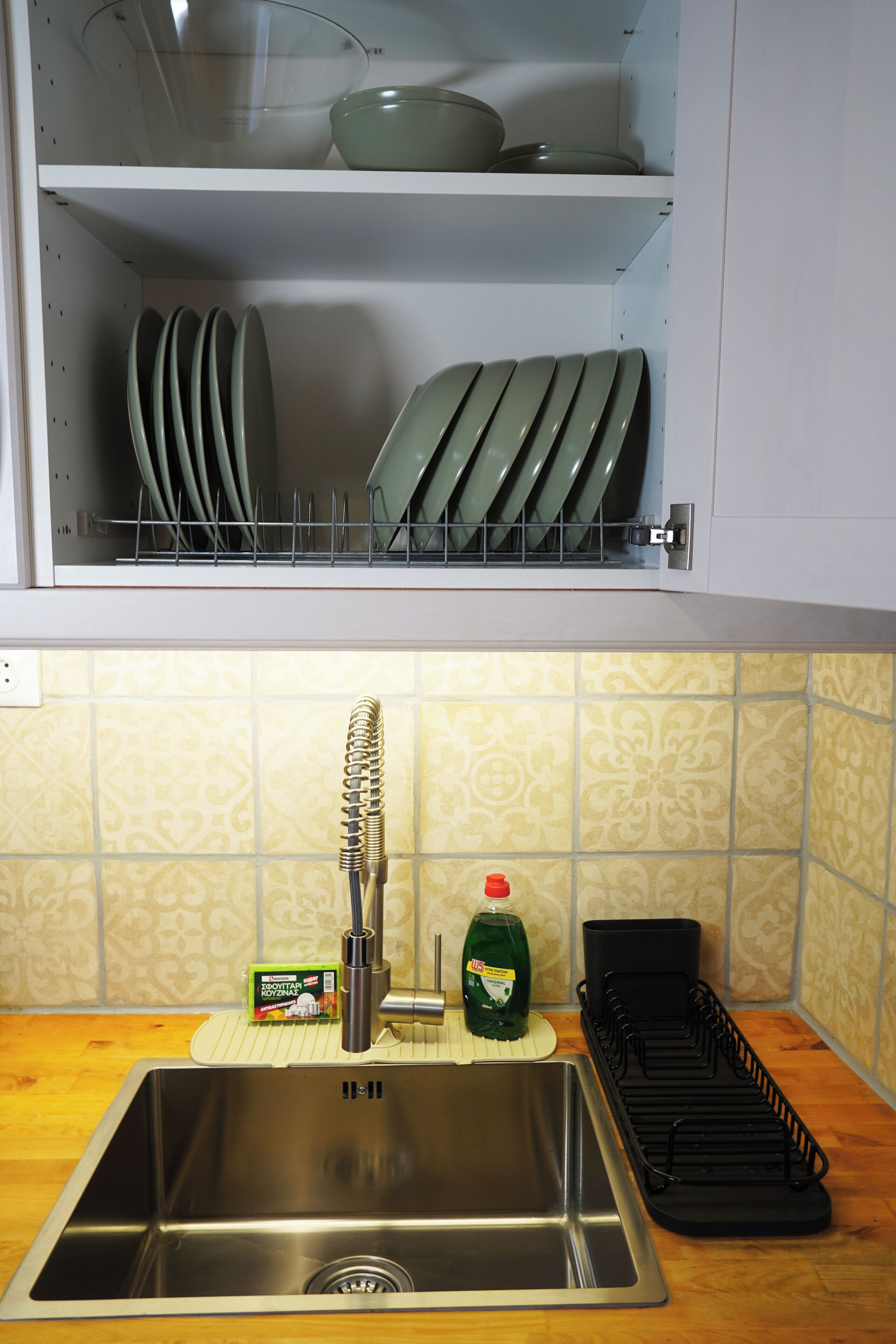 Uma cozinha com uma pia de aço inoxidável, escorredor de louça e um frasco de detergente.