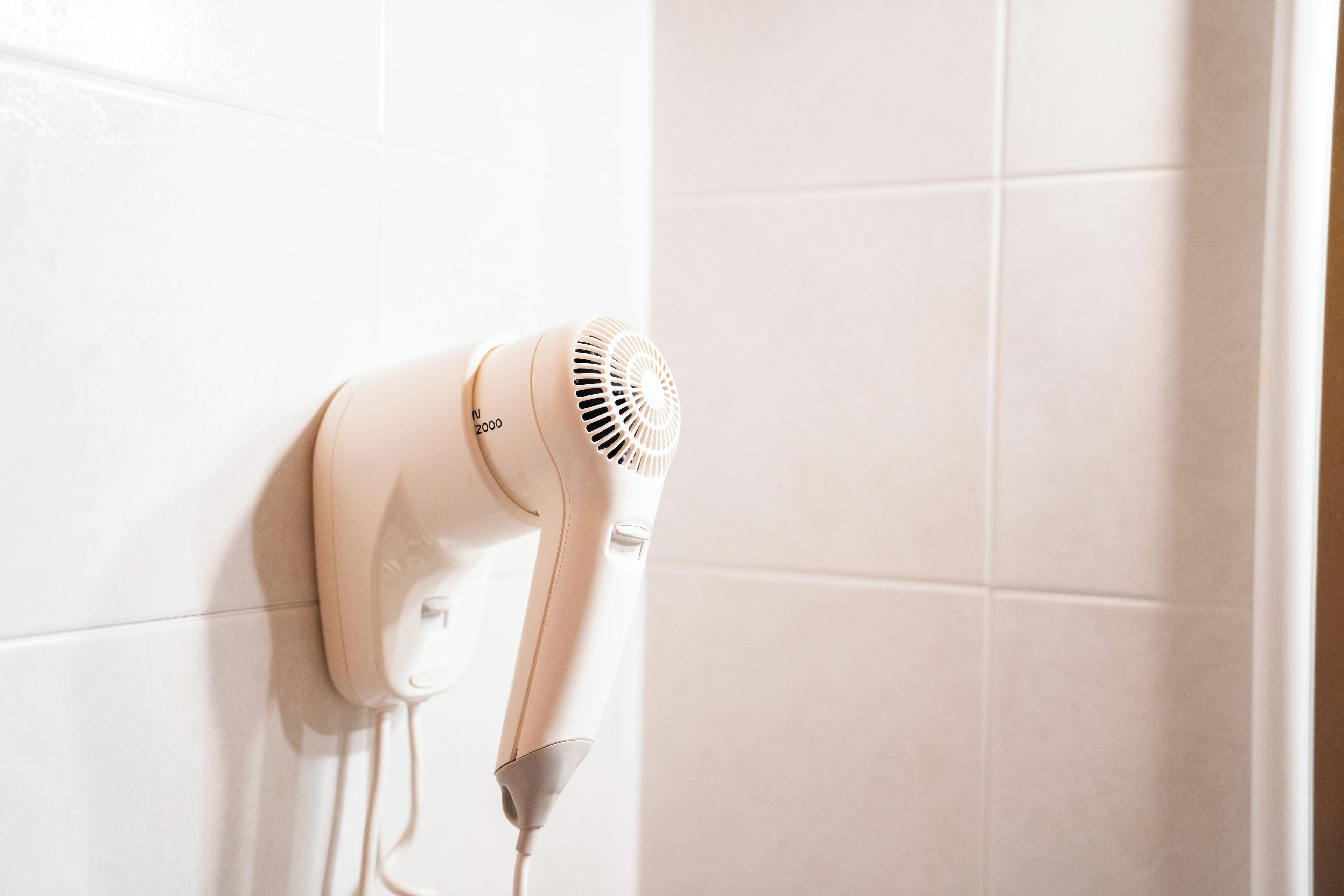Secador de cabelo fixado numa parede revestida de azulejos brancos.
