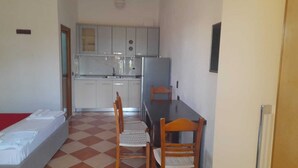 Quarto compacto com cama, uma mesa pequena, duas cadeiras, cozinha compacta e uma janela.
