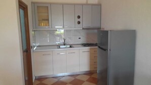 Uma cozinha com armários brancos, uma geladeira de aço inoxidável e piso revestido de azulejos.