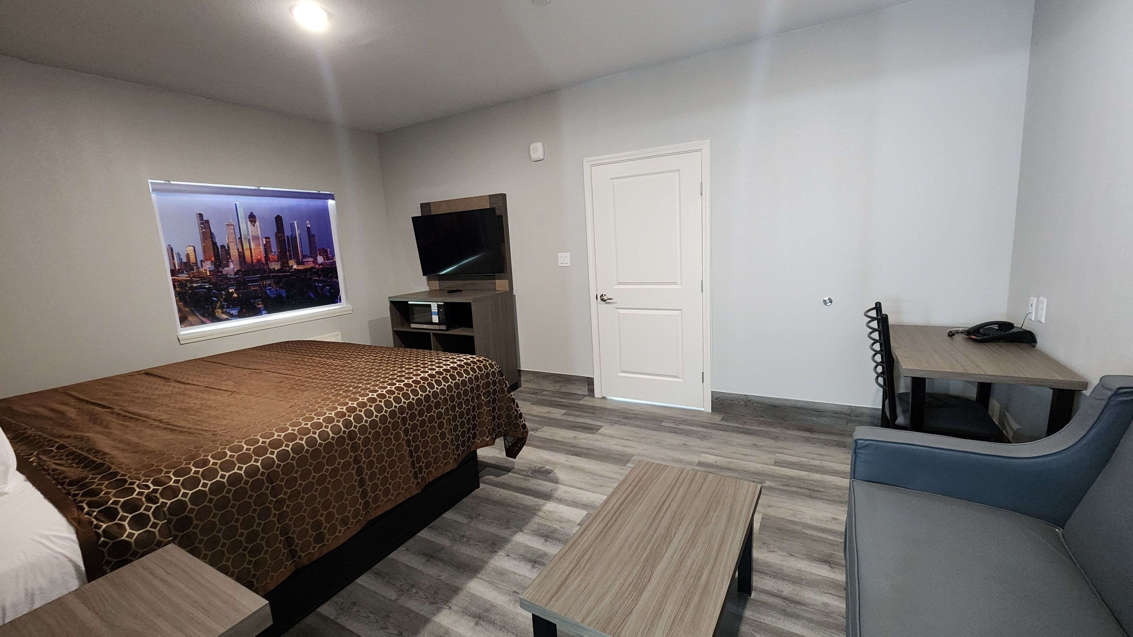 Quarto de hotel com cama, escrivaninha, cadeira, televisão e janela com vista para a cidade.