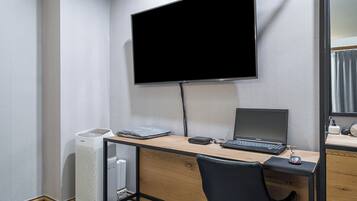 Um espaço de escritório moderno com uma televisão de tela grande, um computador de mesa e um aquecedor vertical.