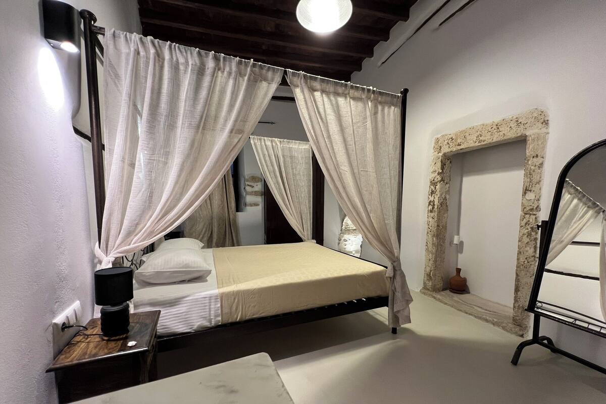 Um quarto com uma cama, mesa de cabeceira, luminária e espelho.