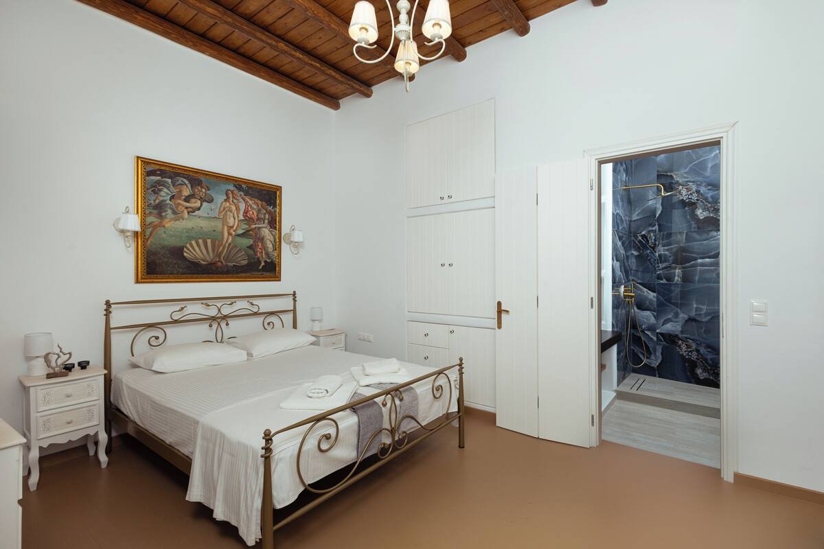 Quarto com cama, mesas de cabeceira, um quadro, guarda-roupa e porta do banheiro.