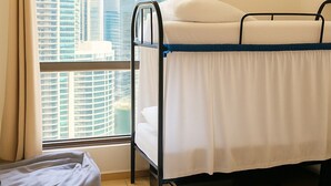 Uma cama de beliche num quarto com vista para a cidade, um pufe redondo e uma lâmpada no teto.