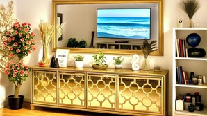 Uma sala de estar com televisão, mesa de apoio com plantas e estante de livros.