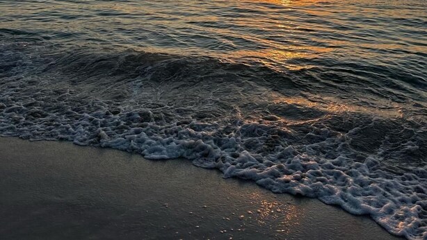 Um pôr do sol sobre a água, com uma grande roda gigante ao fundo.