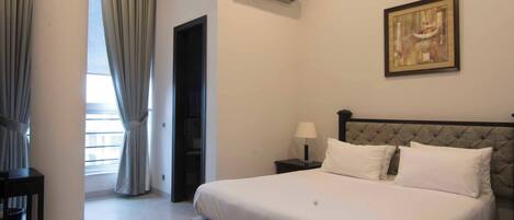 Quarto de hotel moderno com uma cama grande, área de estar com sofá, tapete estampado, ventoinha de teto e um quadro na parede.