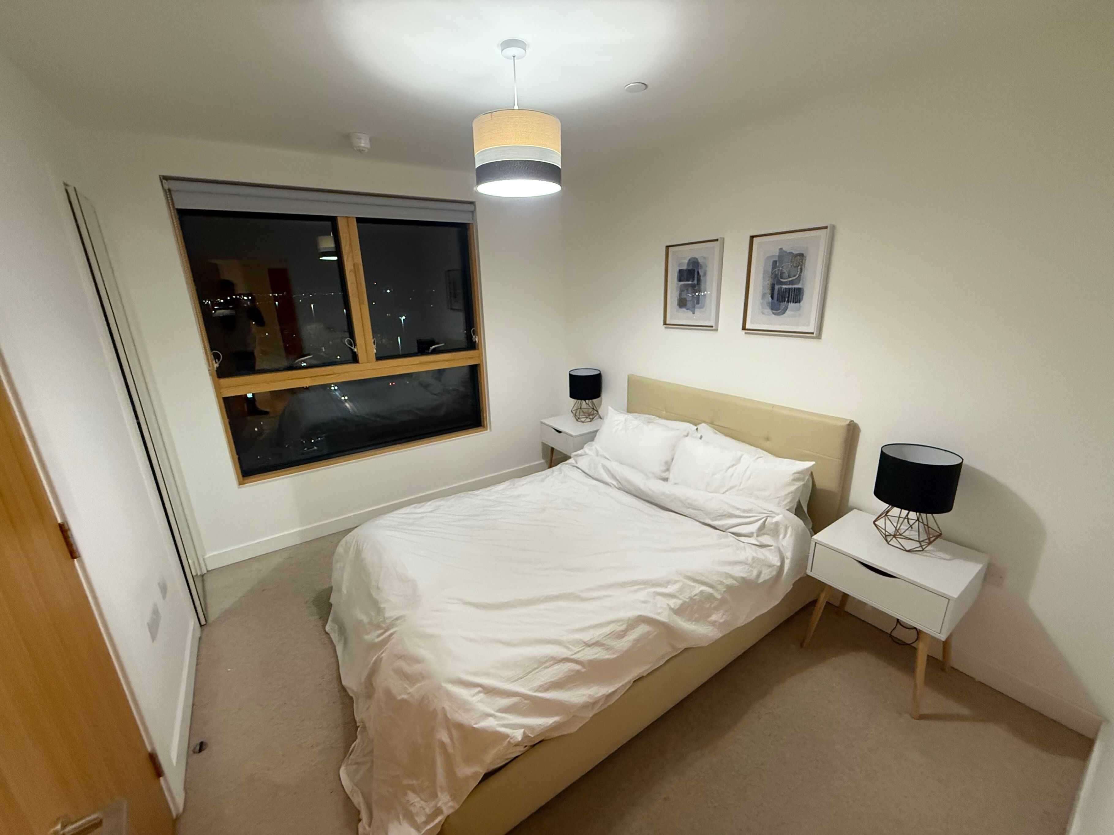 Quarto com cama, janela, duas mesas de cabeceira e duas luminárias fixadas na parede.