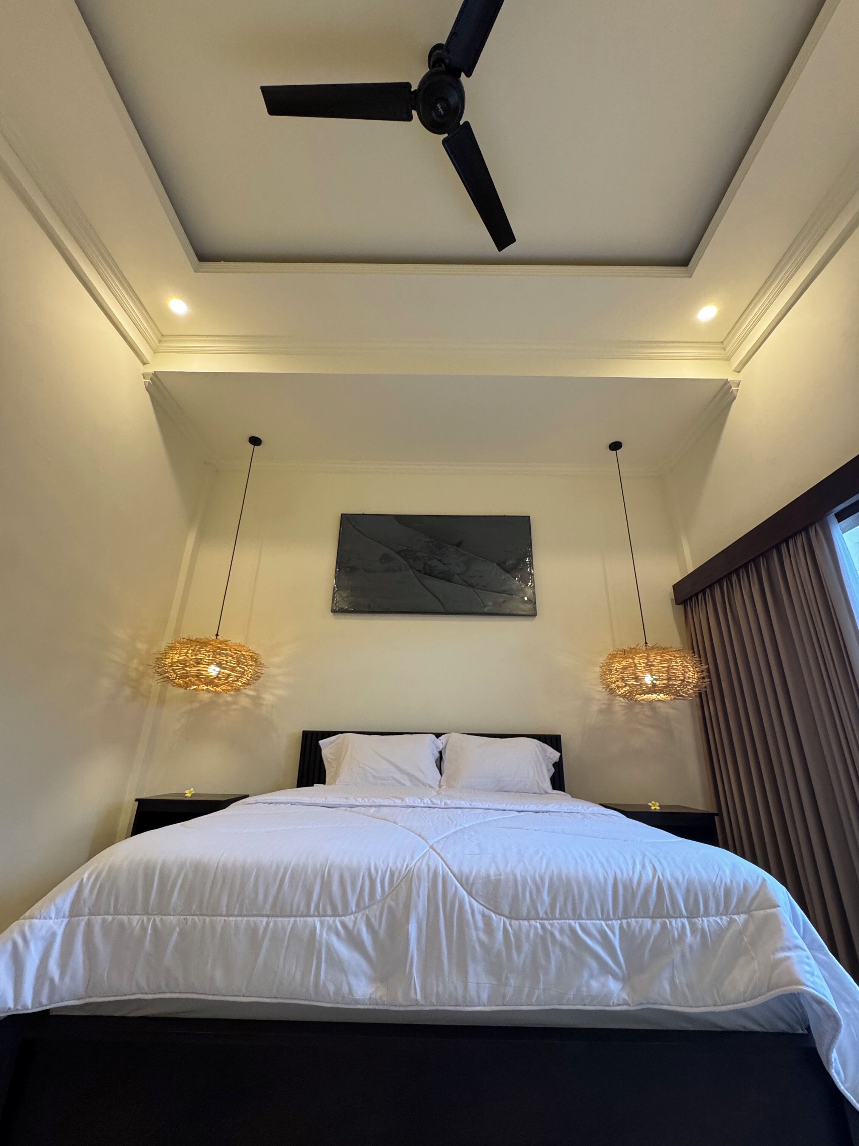 Quarto com cama, ventilador de teto, obra de arte e duas luzes pendentes.