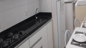 Cozinha com armários brancos, bancada preta, fogão, pia e geladeira.