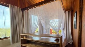 Um quarto de madeira com uma cama, uma janela com cortinas leves e um tapete tecido.