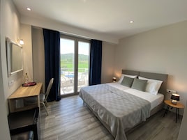 Quarto de hotel com cama, escrivaninha e varanda com mesa e cadeiras.