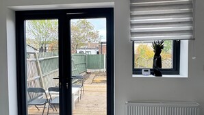 Quarto com porta de vidro deslizante que dá para um deck de madeira, um radiador e uma janela com persiana.