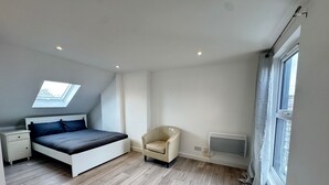 Um quarto com cama, cadeira, claraboia, radiador e janela.