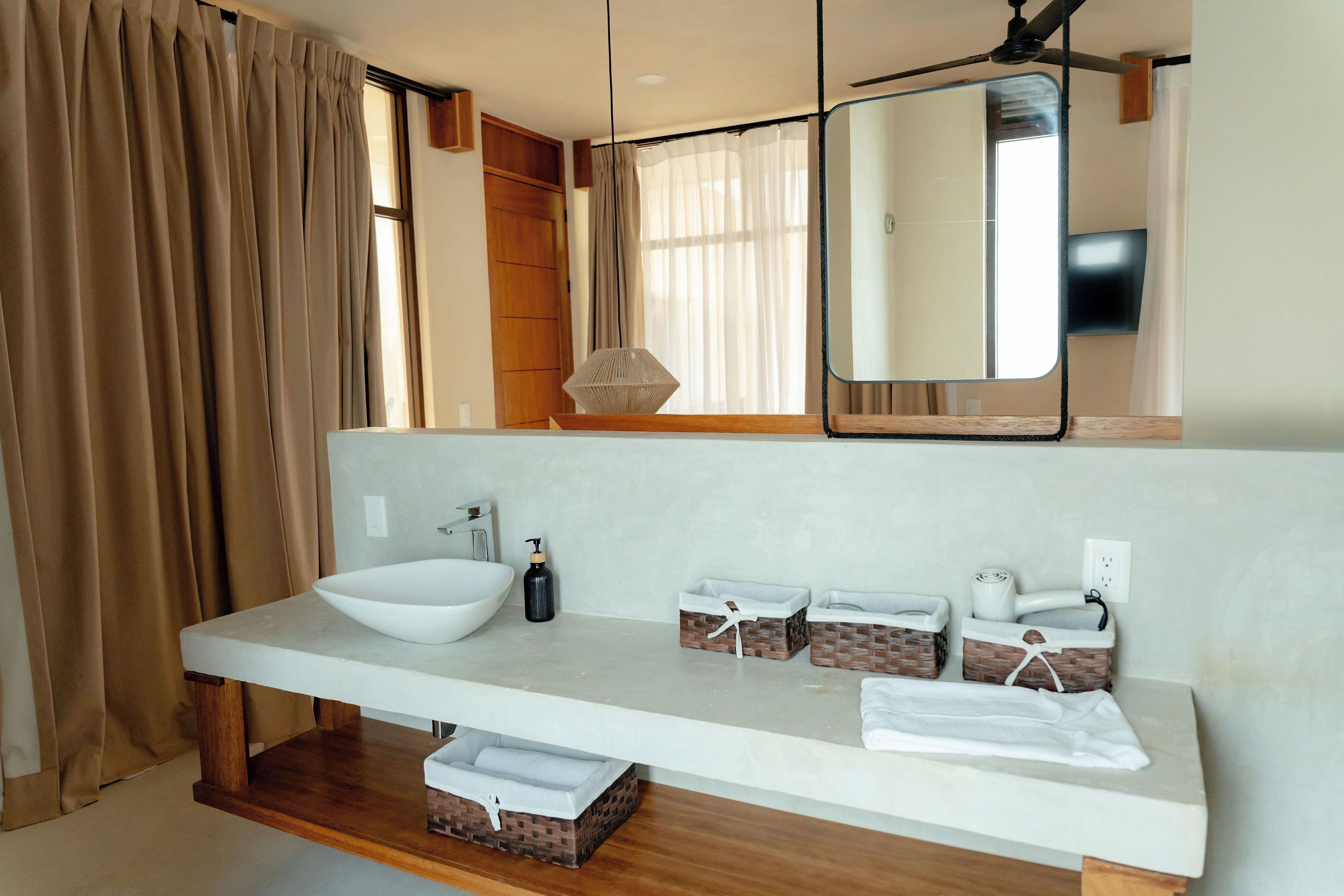 Uma casa de banho moderna com um espelho grande, uma pia branca e prateleiras de madeira.