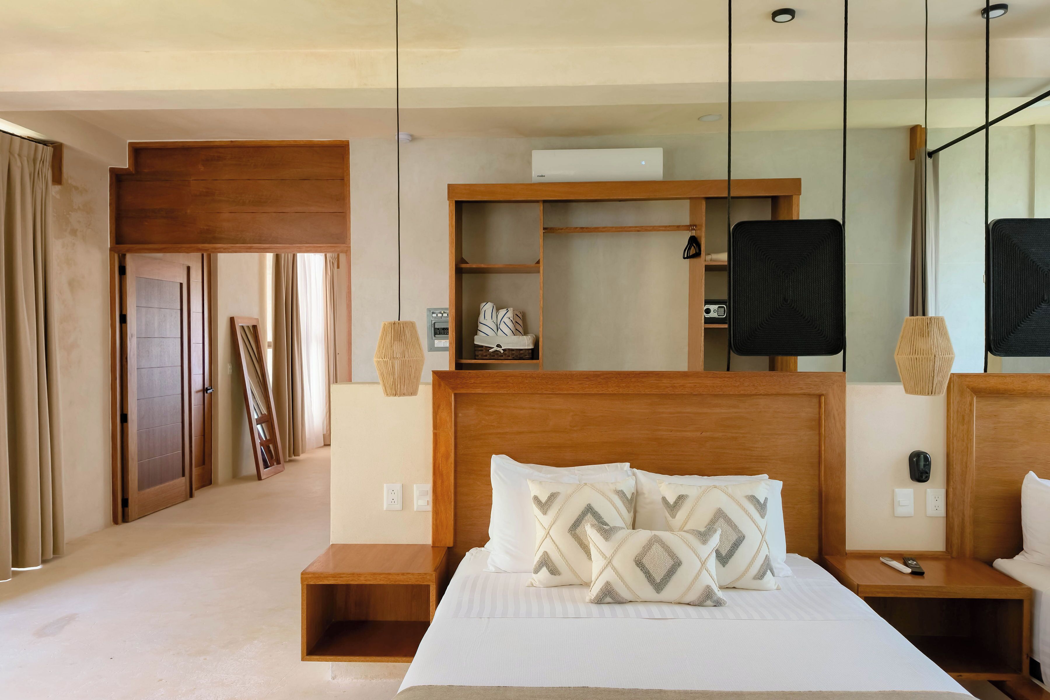 Quarto moderno com cabeceira de madeira, cama grande com almofadas estampadas, mesas de cabeceira e prateleira embutida acima da cama.