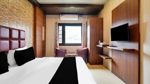 Quarto de hotel com cama grande, televisão de tela plana, mesa pequena e janela com cortinas.