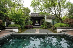 Um edifício em estilo japonês tradicional com telhado de telhas, rodeado por vegetação exuberante e um lago de carpas em primeiro plano.