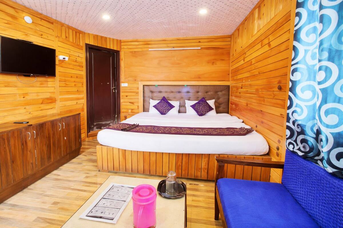 Quarto de madeira com cama, televisão, sofá e mesa com uma garrafa de água e copos.