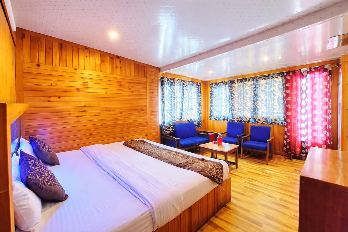 Quarto com cama, duas cadeiras azuis, uma mesinha e cortinas estampadas com flores.
