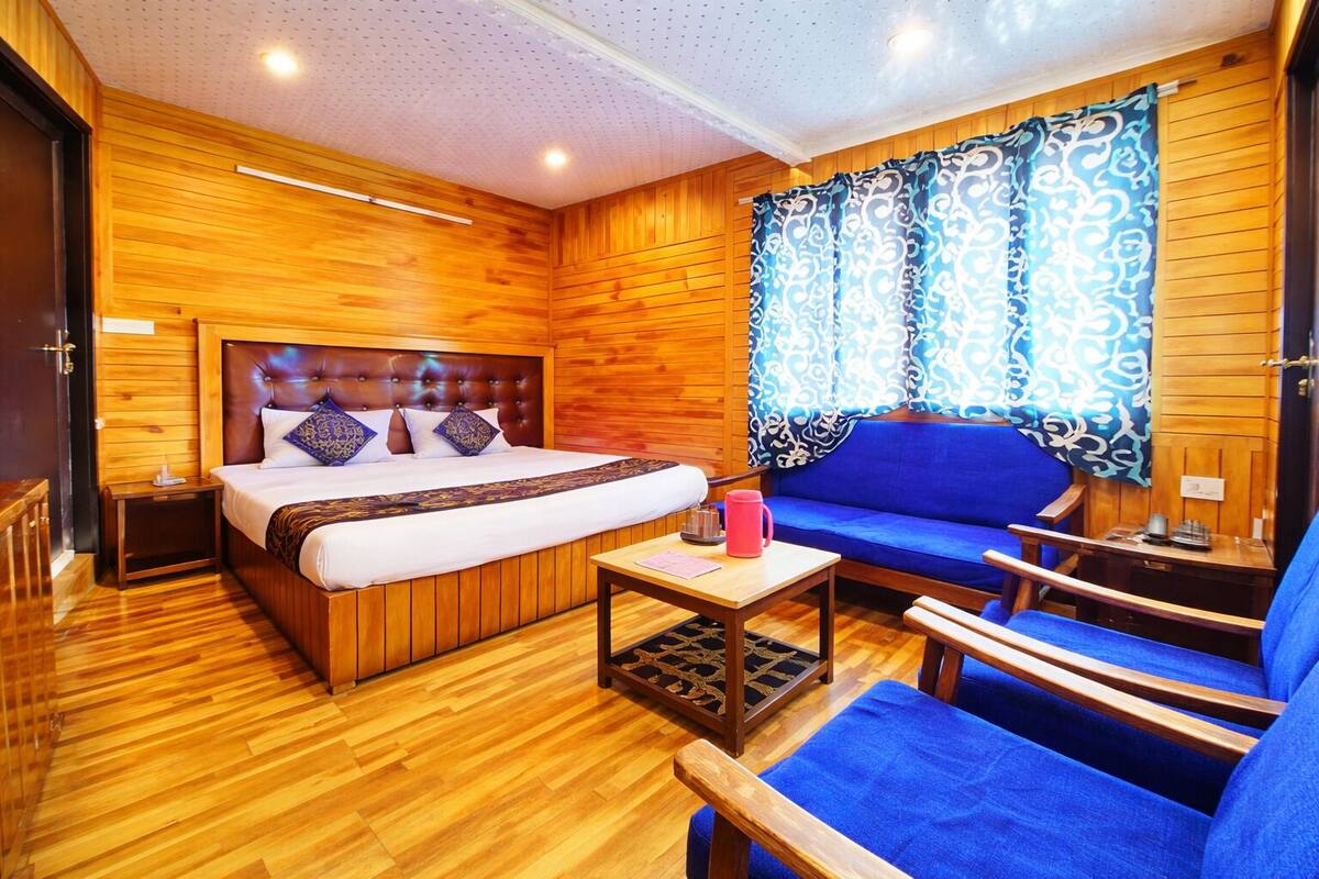 Um quarto com painéis de madeira, uma cama, um sofá azul, uma pequena mesa e uma cadeira.