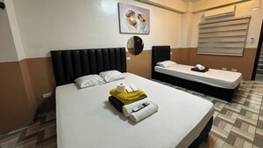 Quarto de hotel com uma cama grande, duas camas menores, um quadro na parede e um aparelho de ar condicionado.