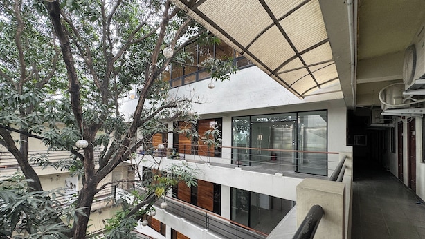 Um edifício com vários andares, fachada de vidro, detalhes em madeira e área externa coberta com árvores.