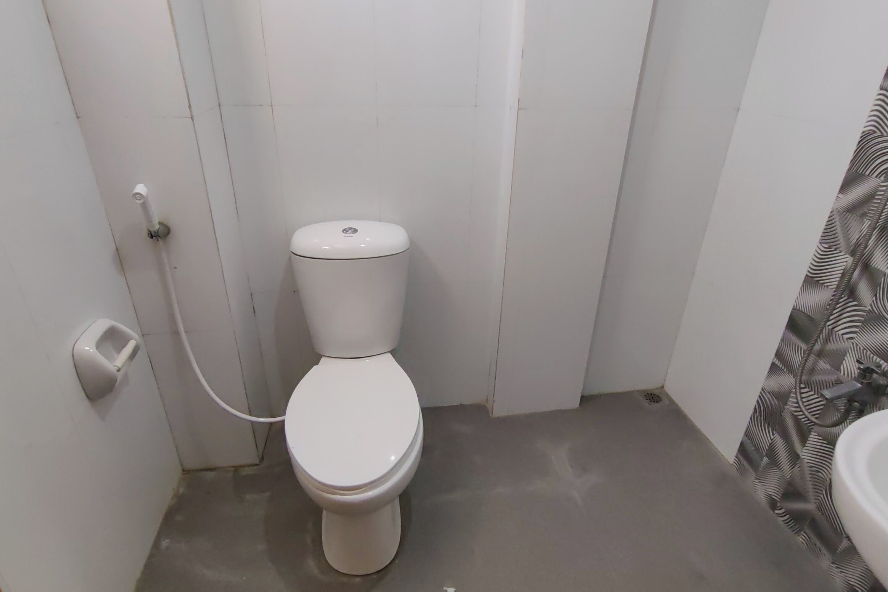 Casa de banho pequena e compacta, com sanita branca, secador de mãos e cortina de chuveiro estampada.