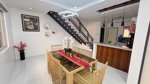 Uma área de jantar moderna com mesa de vidro, cadeiras de vime e escada para um andar superior.