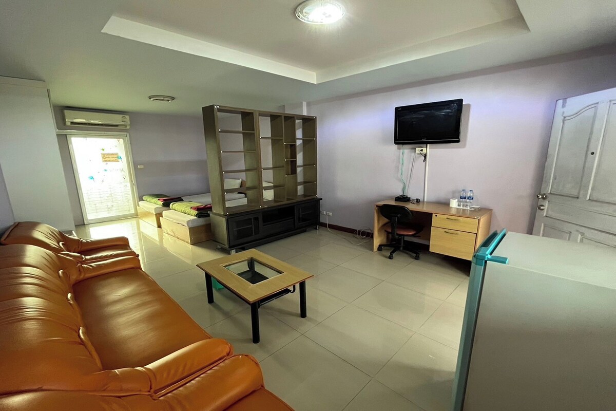 Uma sala de estar com sofá, televisão, escrivaninha e estante de livros.