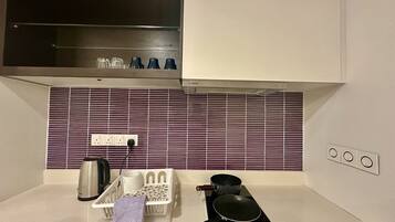Uma cozinha com design moderno, apresentando um exaustor de aço inoxidável, painel de azulejos, chaleira, escorredor de louça e uma frigideira sobre uma placa de indução.