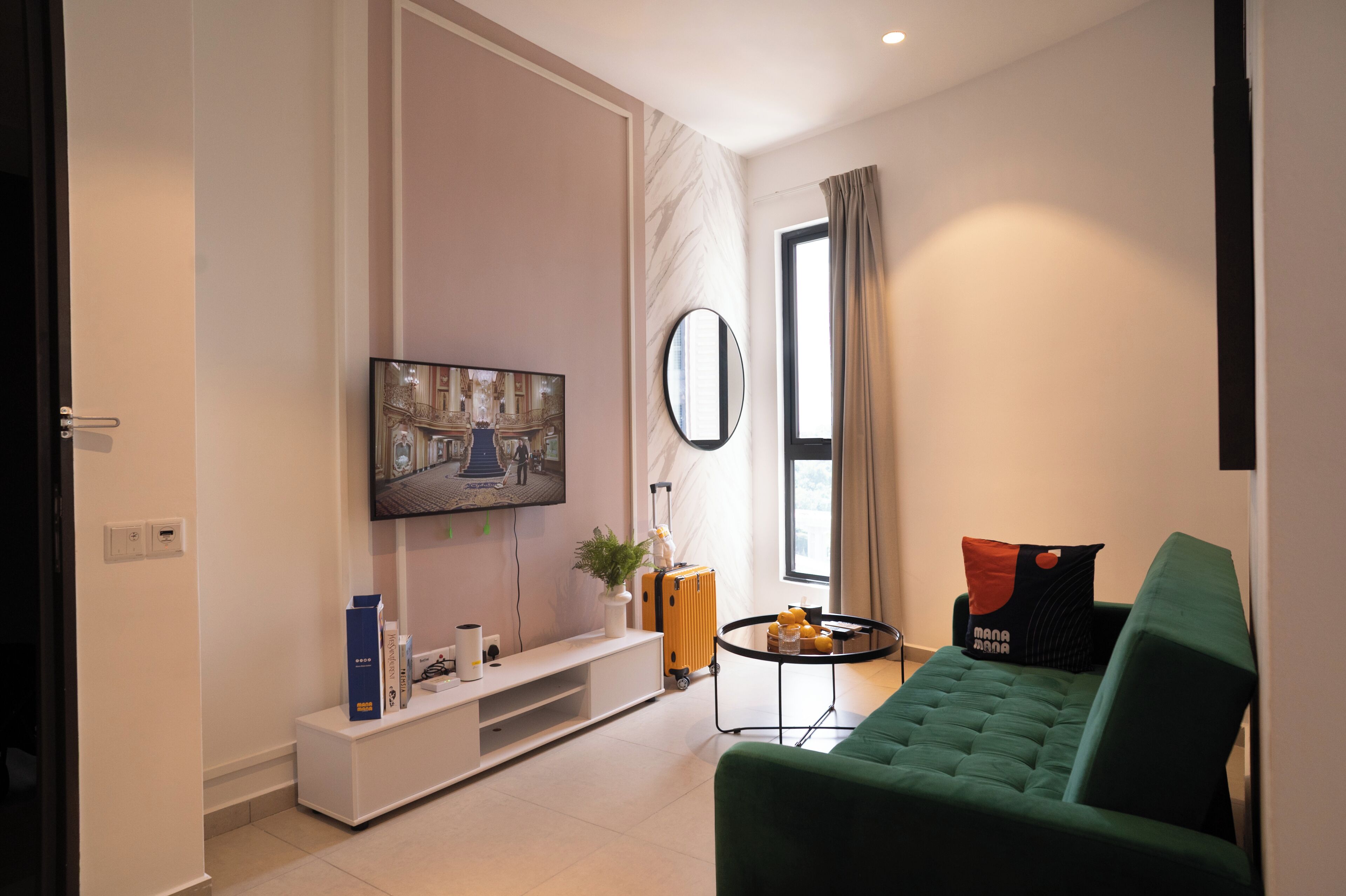 Uma sala de estar moderna com um sofá verde, uma TV de tela plana na parede, uma mesinha lateral e uma janela com cortinas.