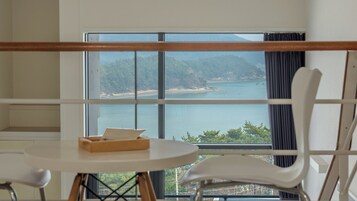 Quarto com vista para a água e colinas, uma mesa redonda com um tabuleiro e uma cadeira branca.