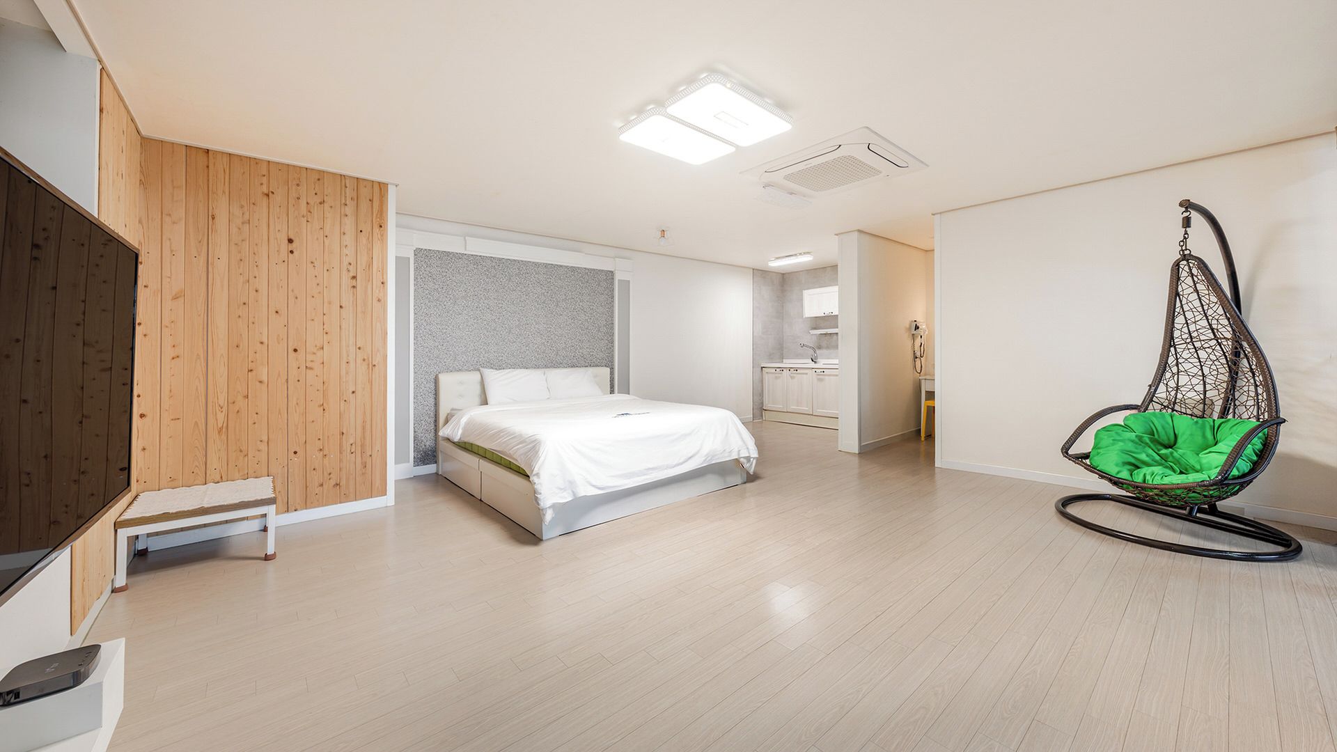 Quarto moderno com cama, cadeira suspensa e kitchenette.
