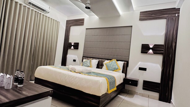 Quarto de hotel moderno com cama grande, mesas de cabeceira, ar condicionado e luminária no teto.