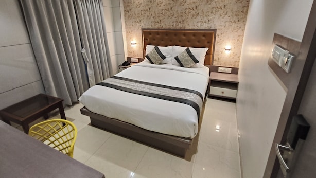 Quarto de hotel moderno com uma cama grande, uma mesa de cabeceira, um criado-mudo e uma cadeira, além de um aparelho de ar condicionado.