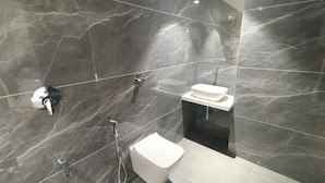 Um banheiro moderno com azulejos de mármore escuro, pia branca, vaso sanitário e chuveiro.