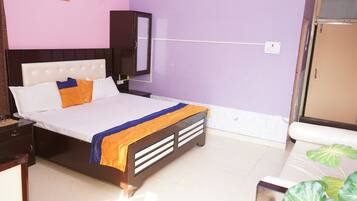 Uma cama bem arrumada com colcha branca e azul, cabeceira de madeira e mesa de cabeceira com abajur.