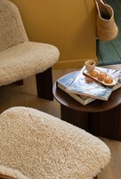 Um quarto aconchegante com uma mesa de madeira redonda, uma revista, uma xícara e um prato de biscoitos.