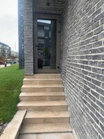 Degraus de concreto levam a uma porta de vidro na entrada de um edifício com fachada de pedra.