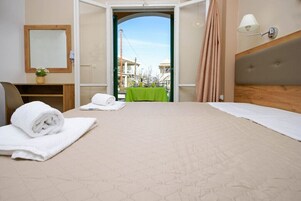 Quarto de hotel com uma cama, uma mesa verde, um espelho e vista para o exterior.