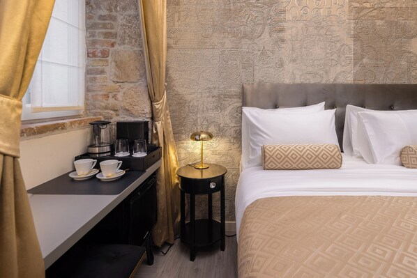 Quarto de hotel com cama, mesa de cabeceira com abajur, cantinho para café e vista para a parede de pedra.