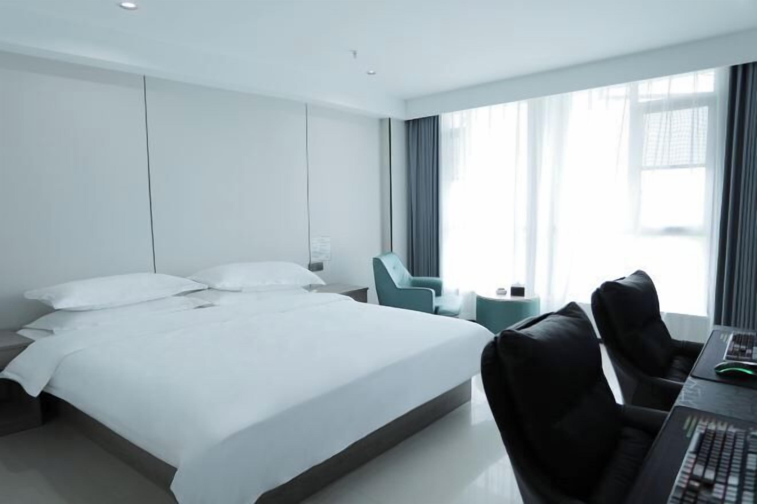 Quarto de hotel com uma cama grande, uma escrivaninha com computador e uma janela com cortinas.