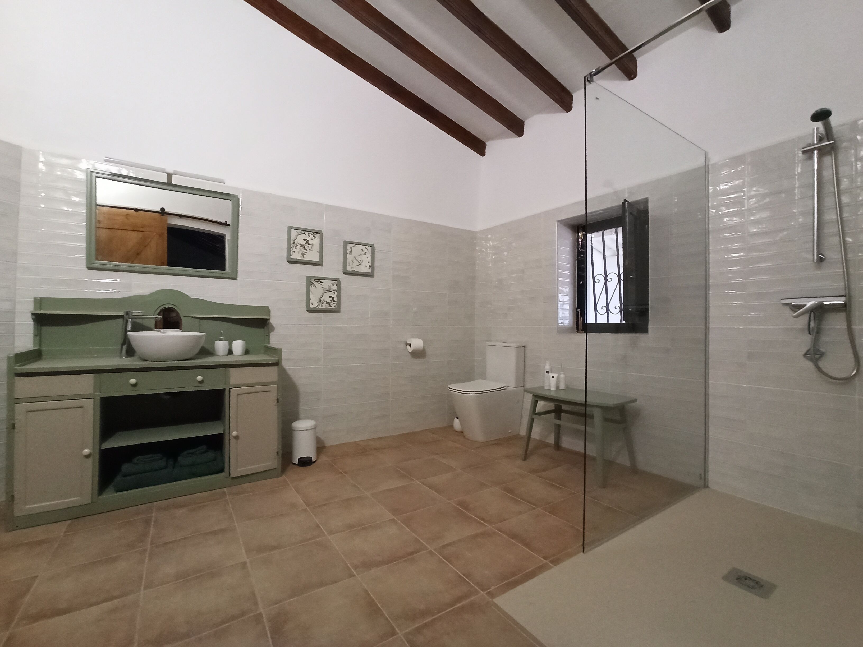 Casa de banho com toucador verde, lavatório branco, sanita e zona de duche com parede de vidro.