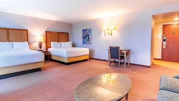 Quarto de hotel com duas camas, uma mesa redonda, uma cadeira, uma secretária pequena e um quadro na parede.